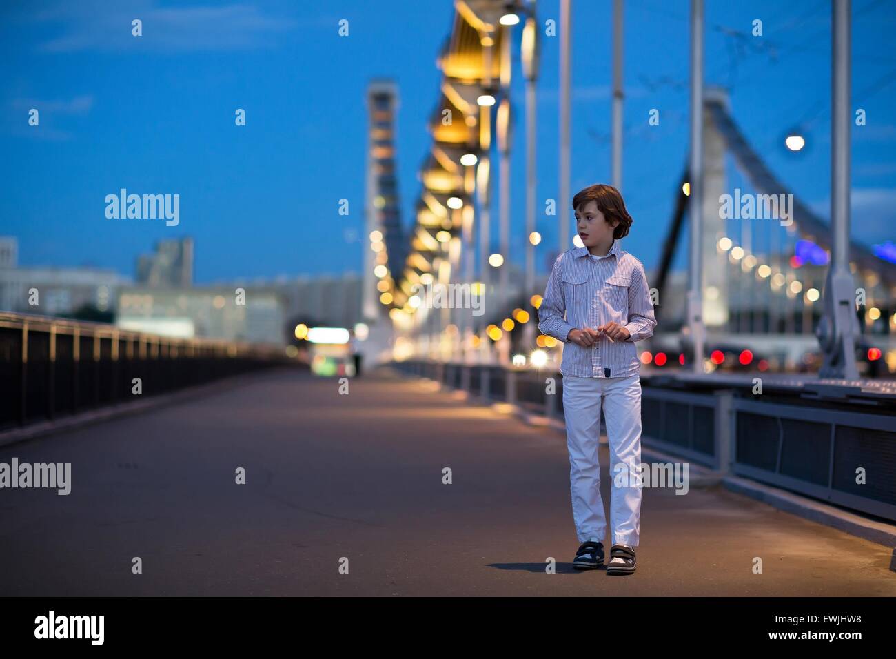 Little boy walking alone scared on a beautiful bridge in a dark city at ...