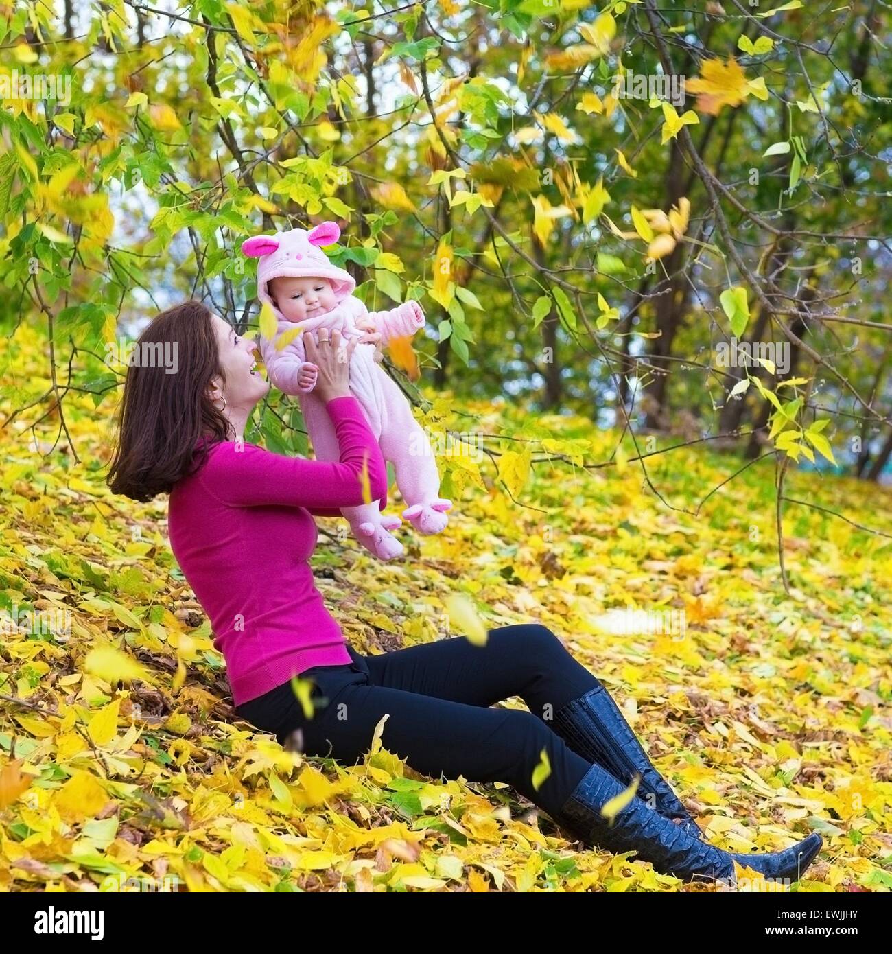 Young mother holding her baby catching falling autumn leaves Stock ...