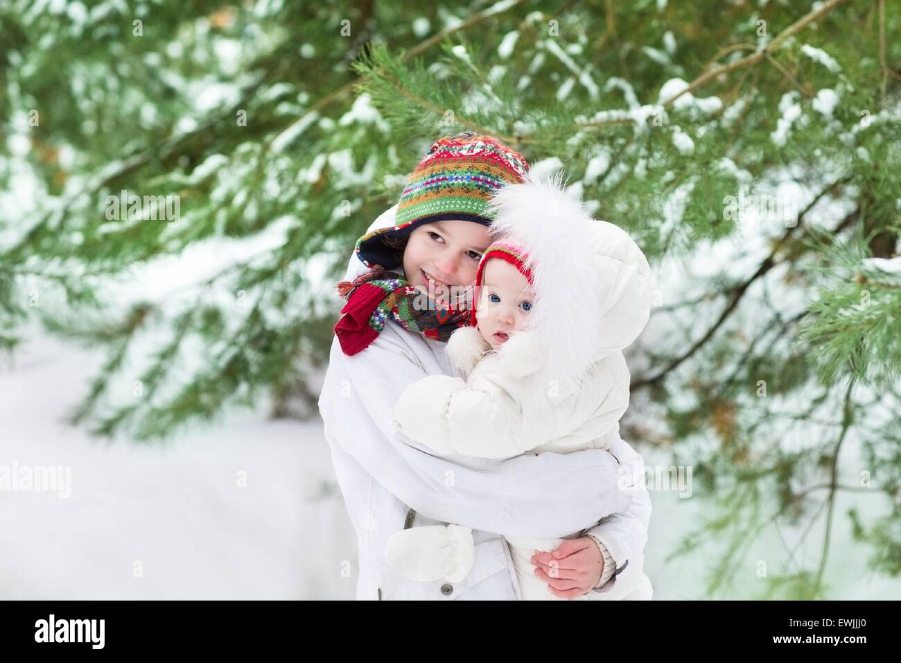 Cute boy hugging his baby sister in a beautiful winter park under a ...