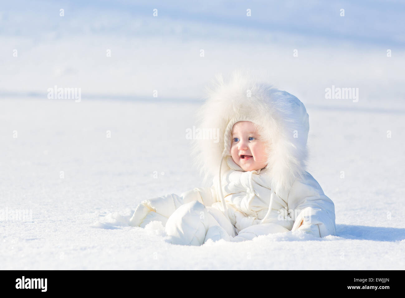 Adorable laughing baby girl in a warm white snow suit playing in snow ...