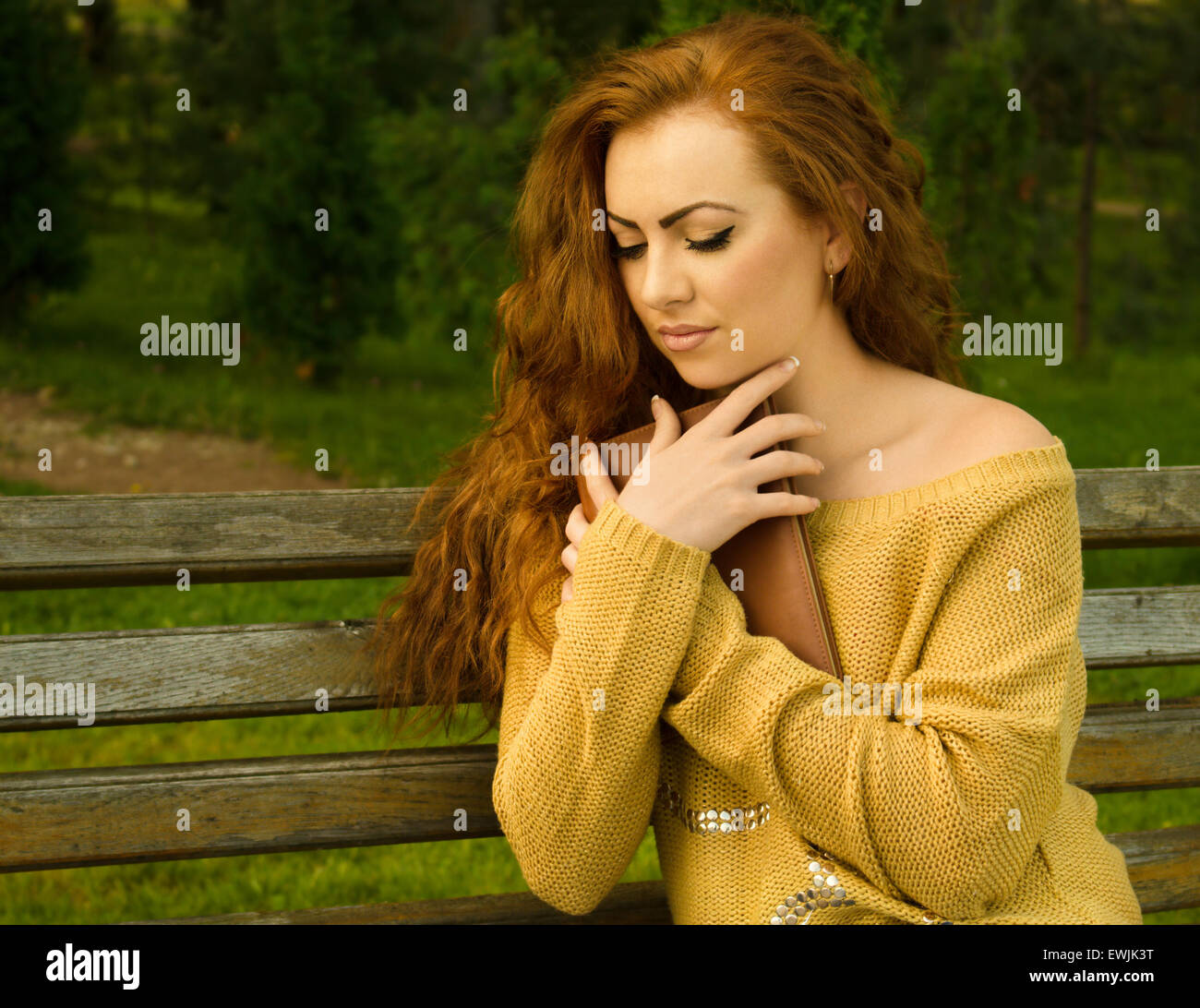 Ginger-haired woman sitting on a bench with book in the park Stock ...