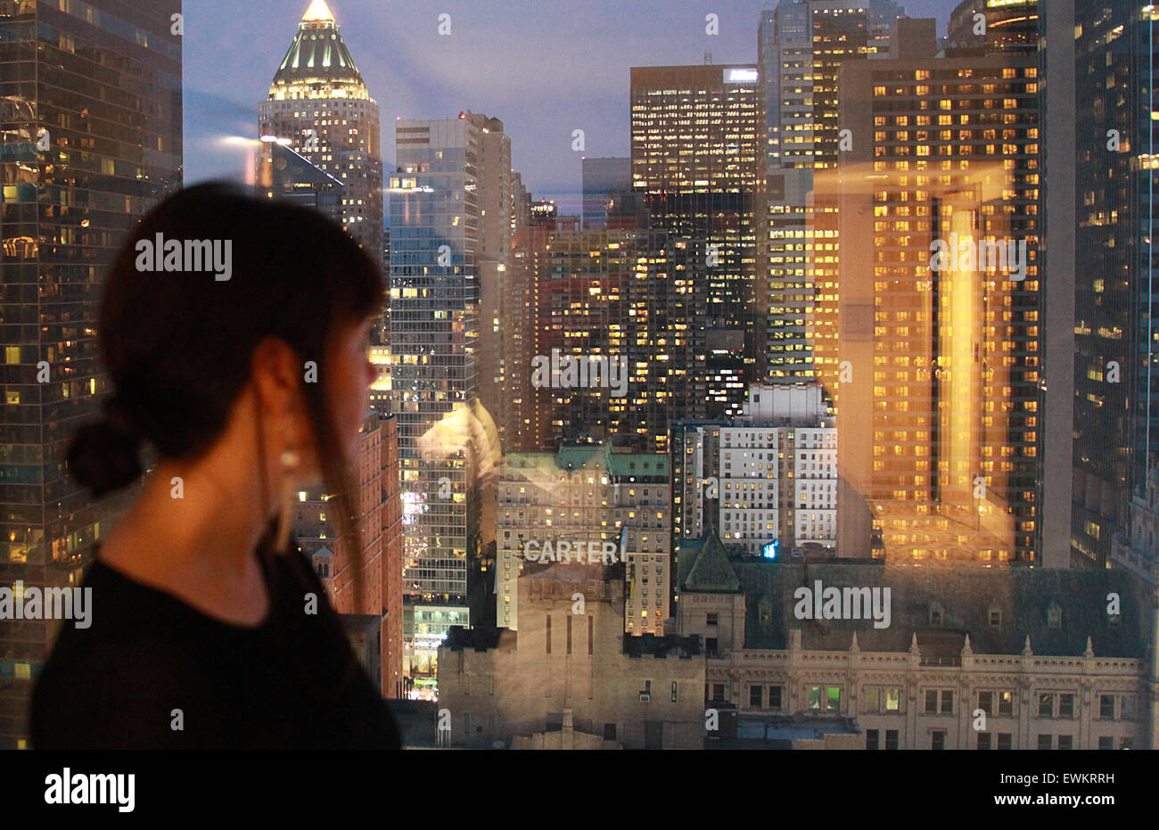 Woman looking out of window at the Manhattan skyline at night with ...