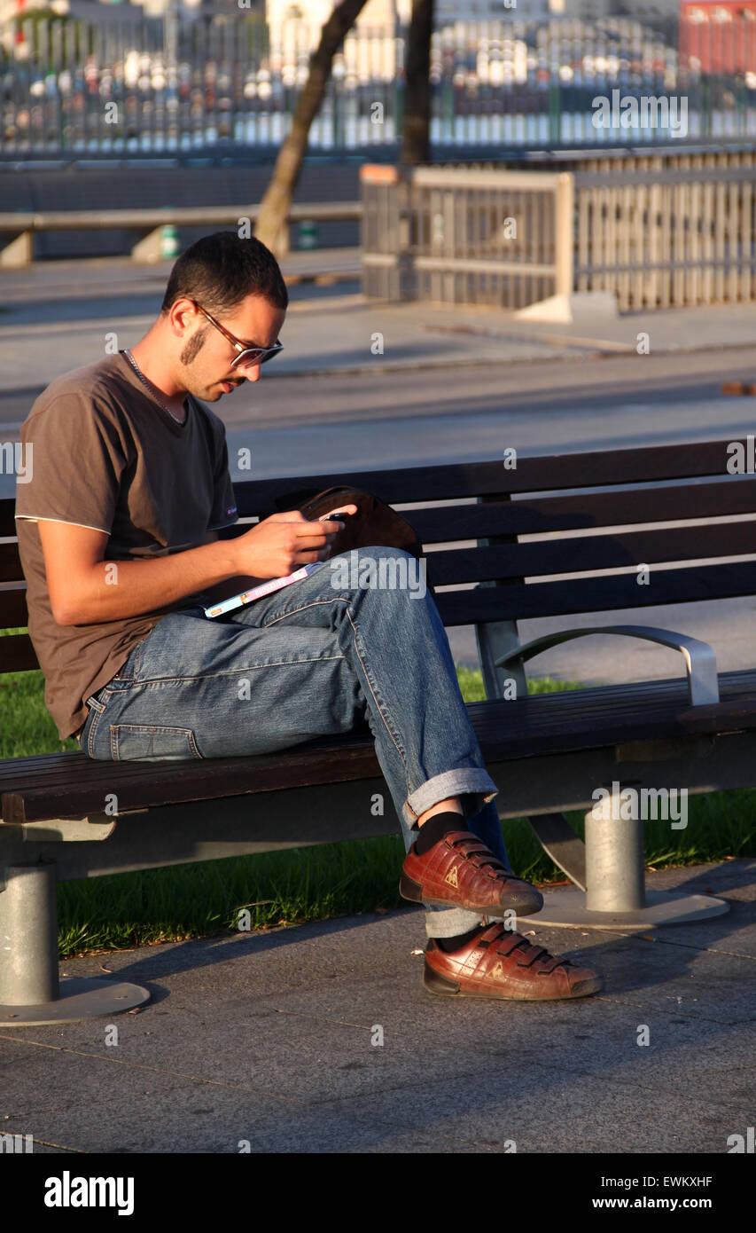 Young man sitting on bench using mobile/cell phone Stock Photo - Alamy