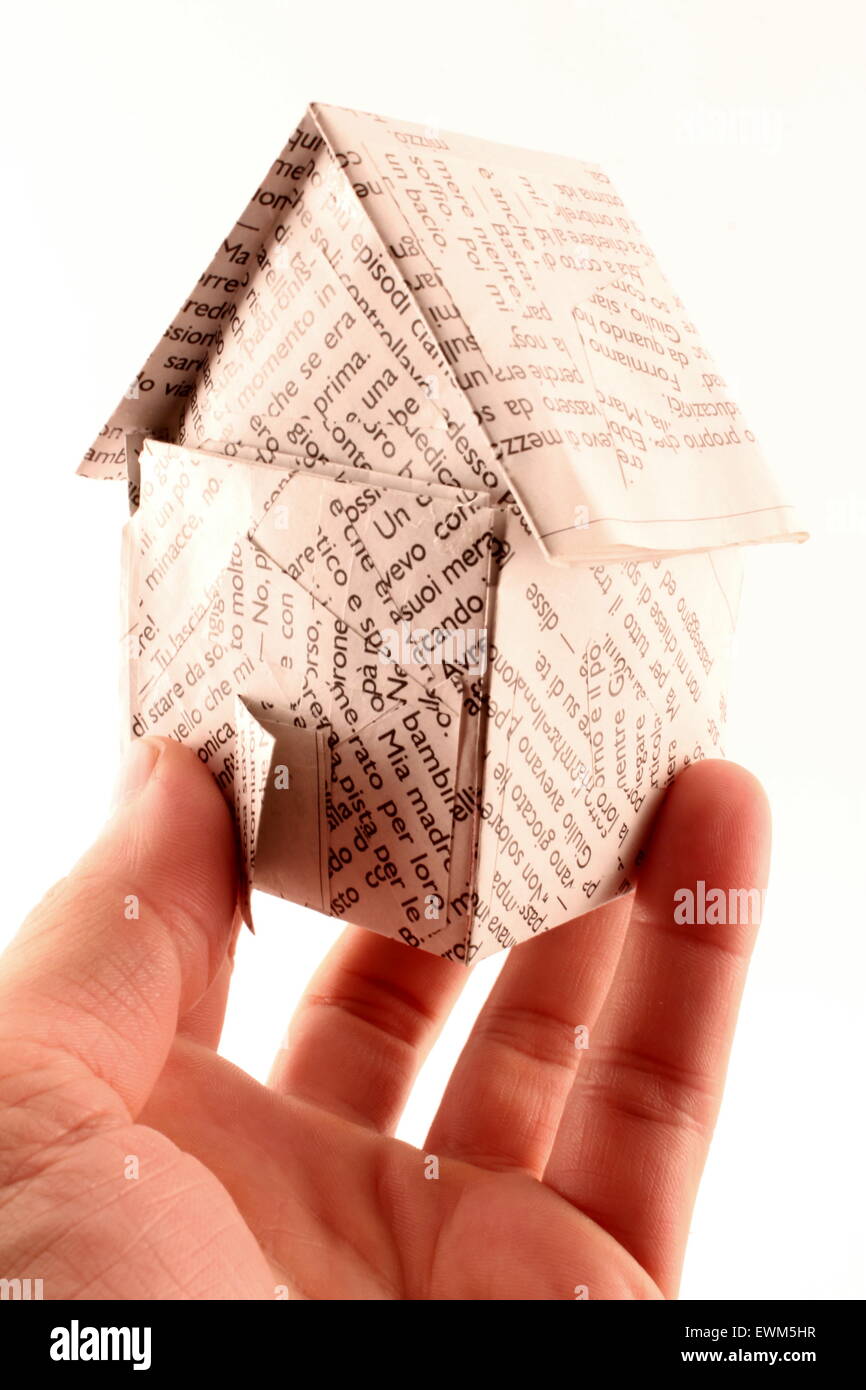 An isolated house, made with paper of a newspaper, Italian. The hand of ...