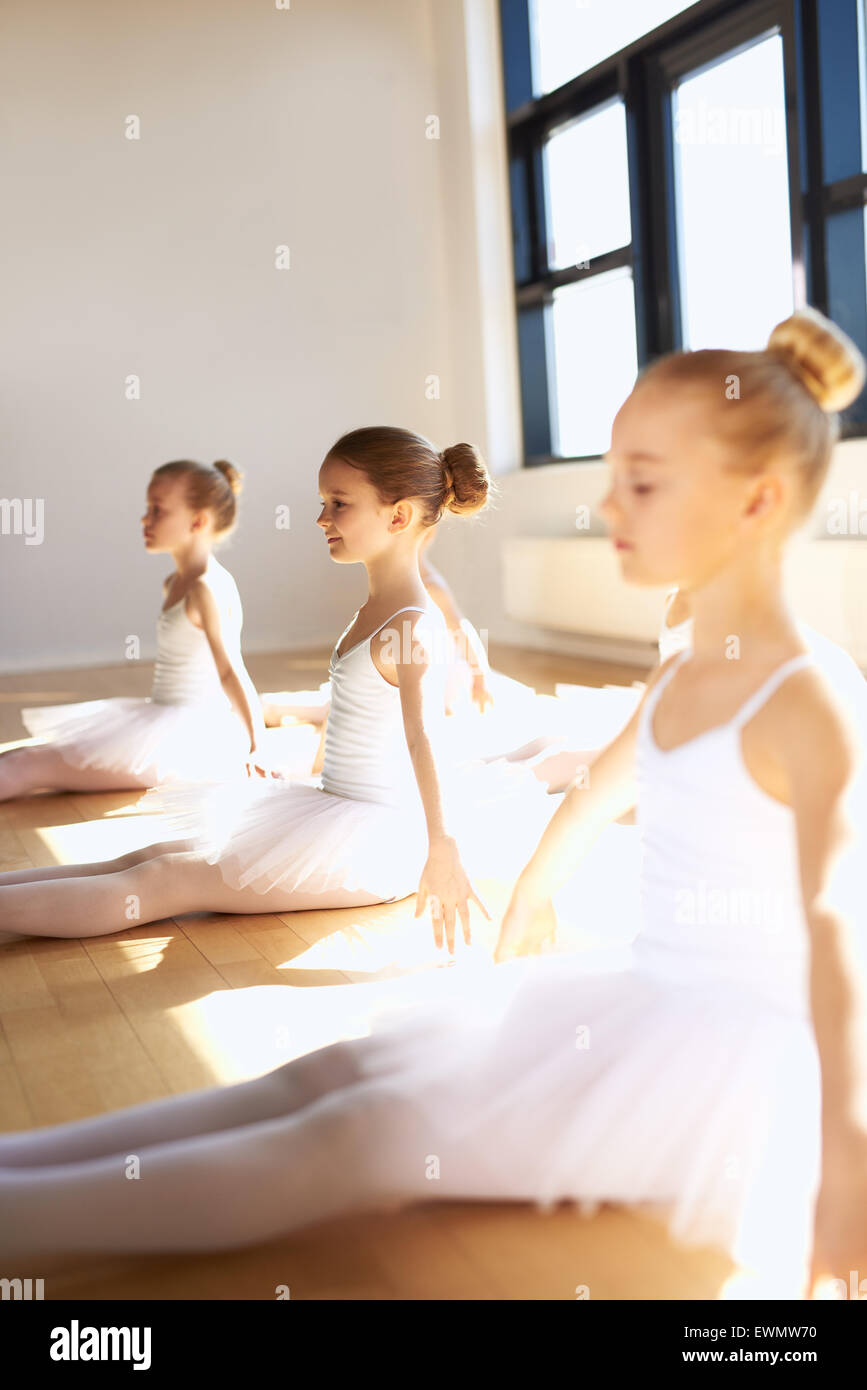 Three young girls in ballet class sitting on a wooden floor in the ...