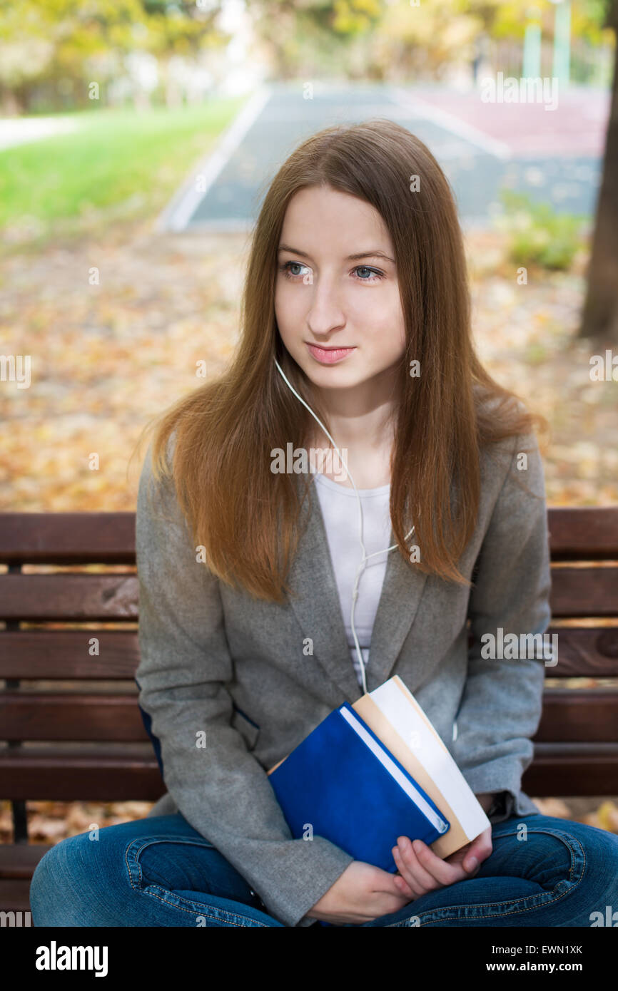 Student sitting on bench with headphones and book in autumn Stock Photo ...