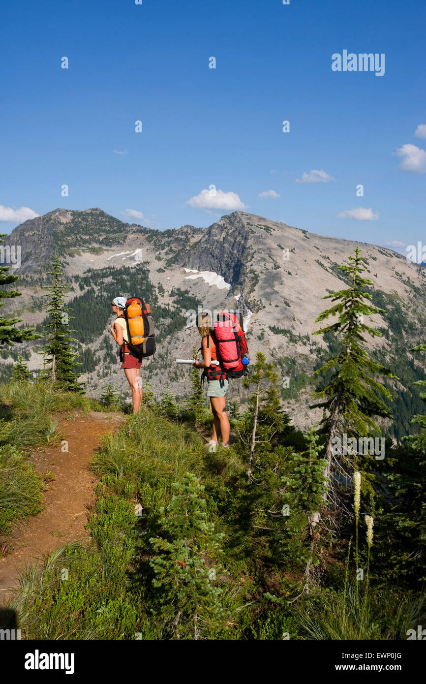 Two adult women backpacking in a wilderness area under a bright blue ...