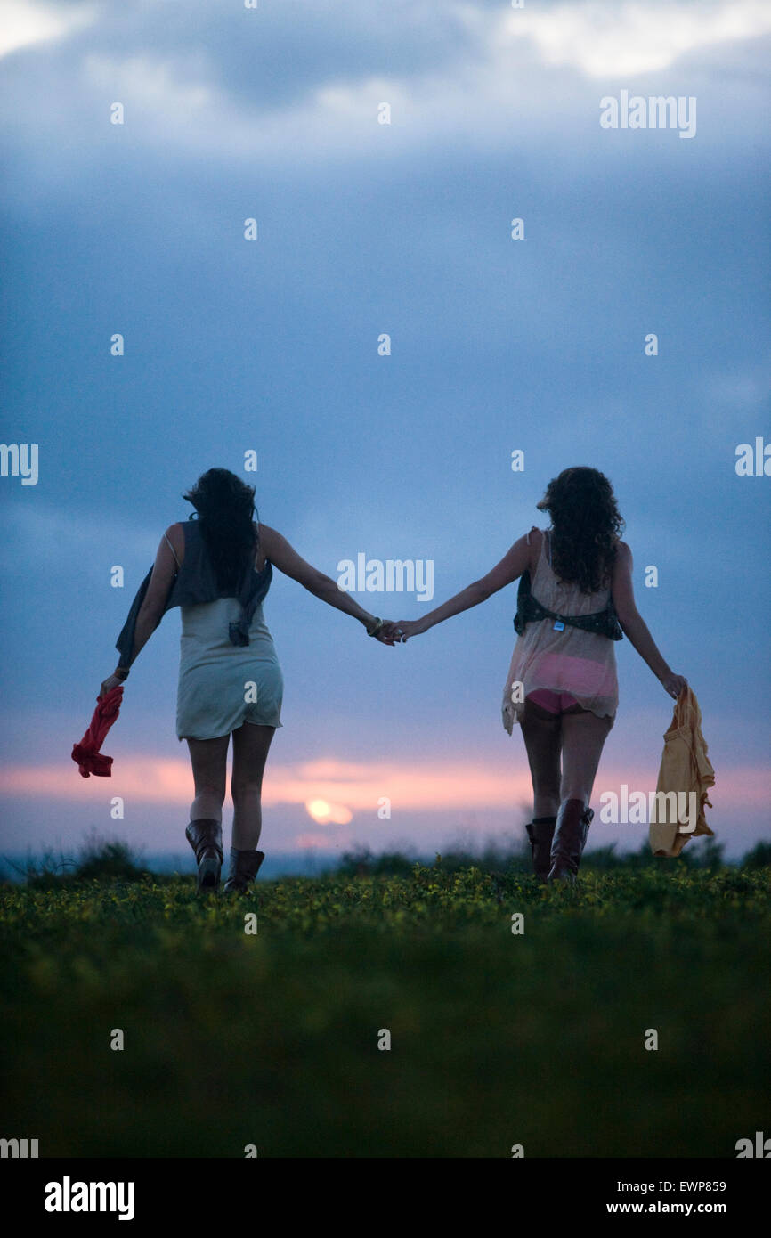 Two adult women walking toward the sunset holding hands Stock Photo - Alamy