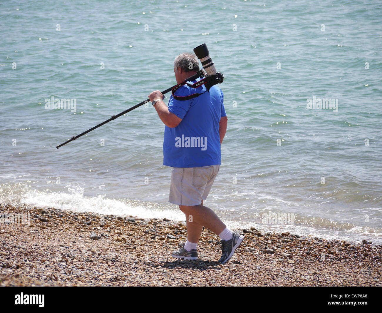 A photographer with a camera on a monopod walks along a beach alone ...