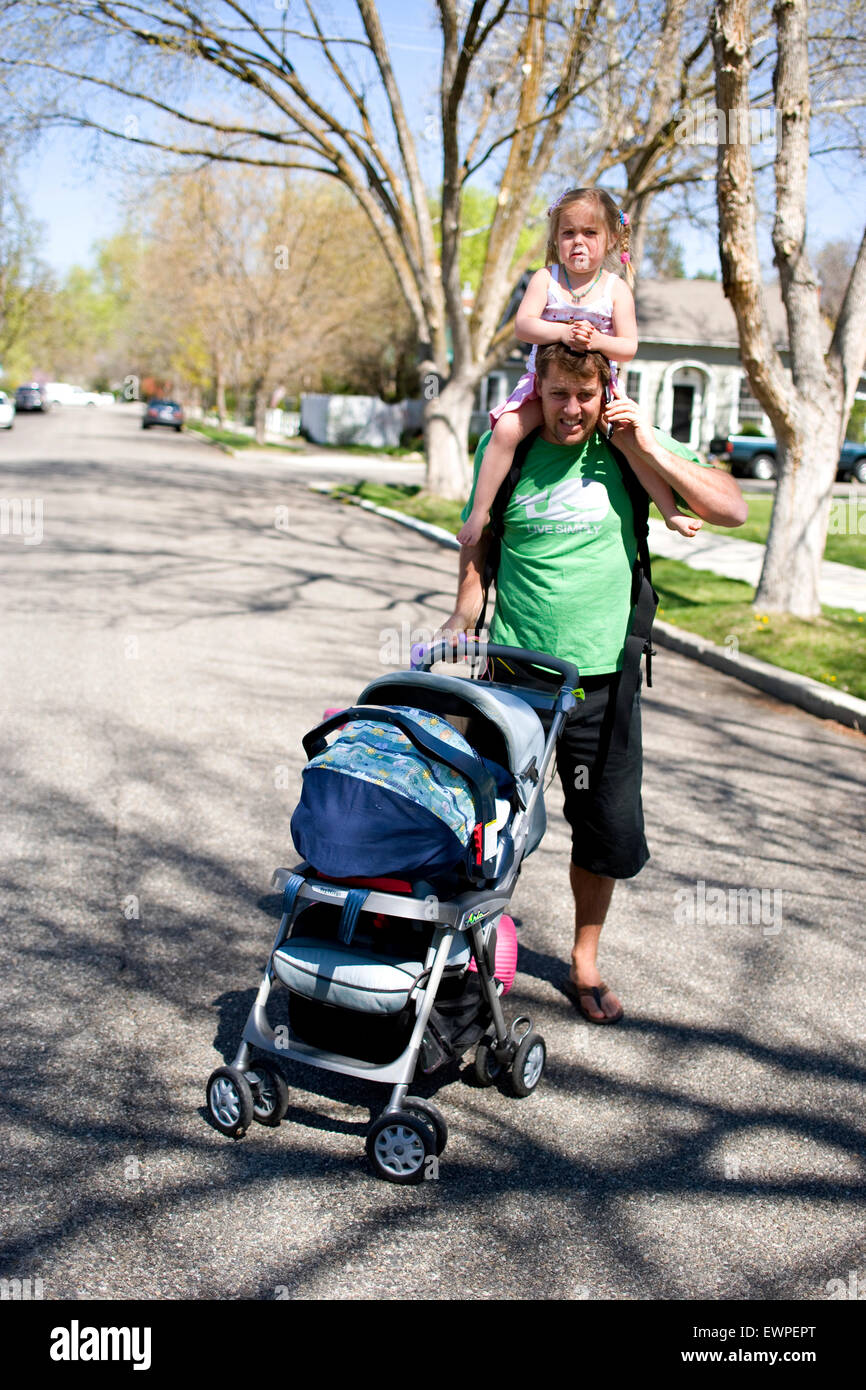Overwhelmed father holding his daughter, pushing a baby stroller, and ...