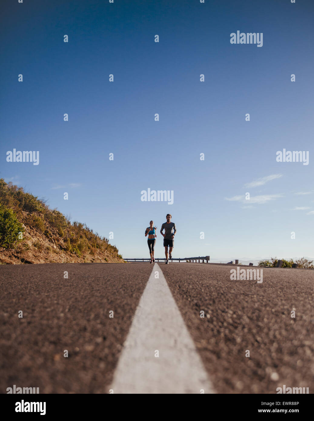 Low angle shot of two young runners training together on the road ...