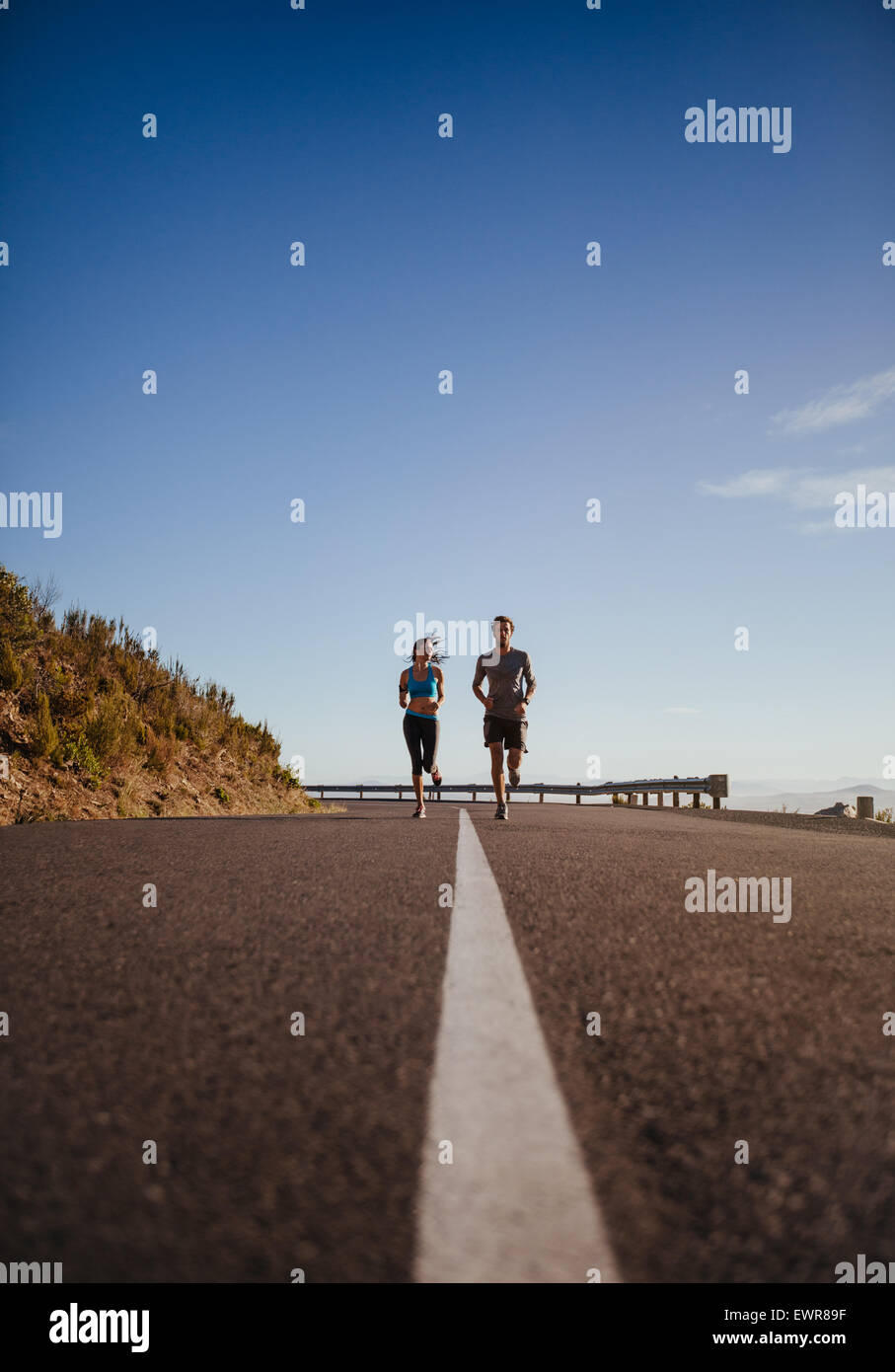 Two young people jogging on country road, low angle distant shot of ...