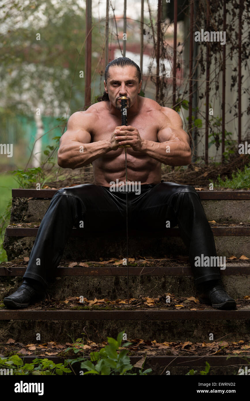 Action Hero Muscled Man Holding A Ancient Sword - Standing In Forest ...