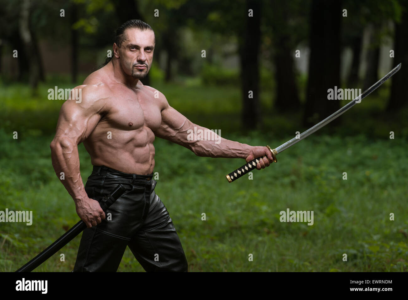 Action Hero Muscled Man Holding A Ancient Sword - Standing In Forest ...