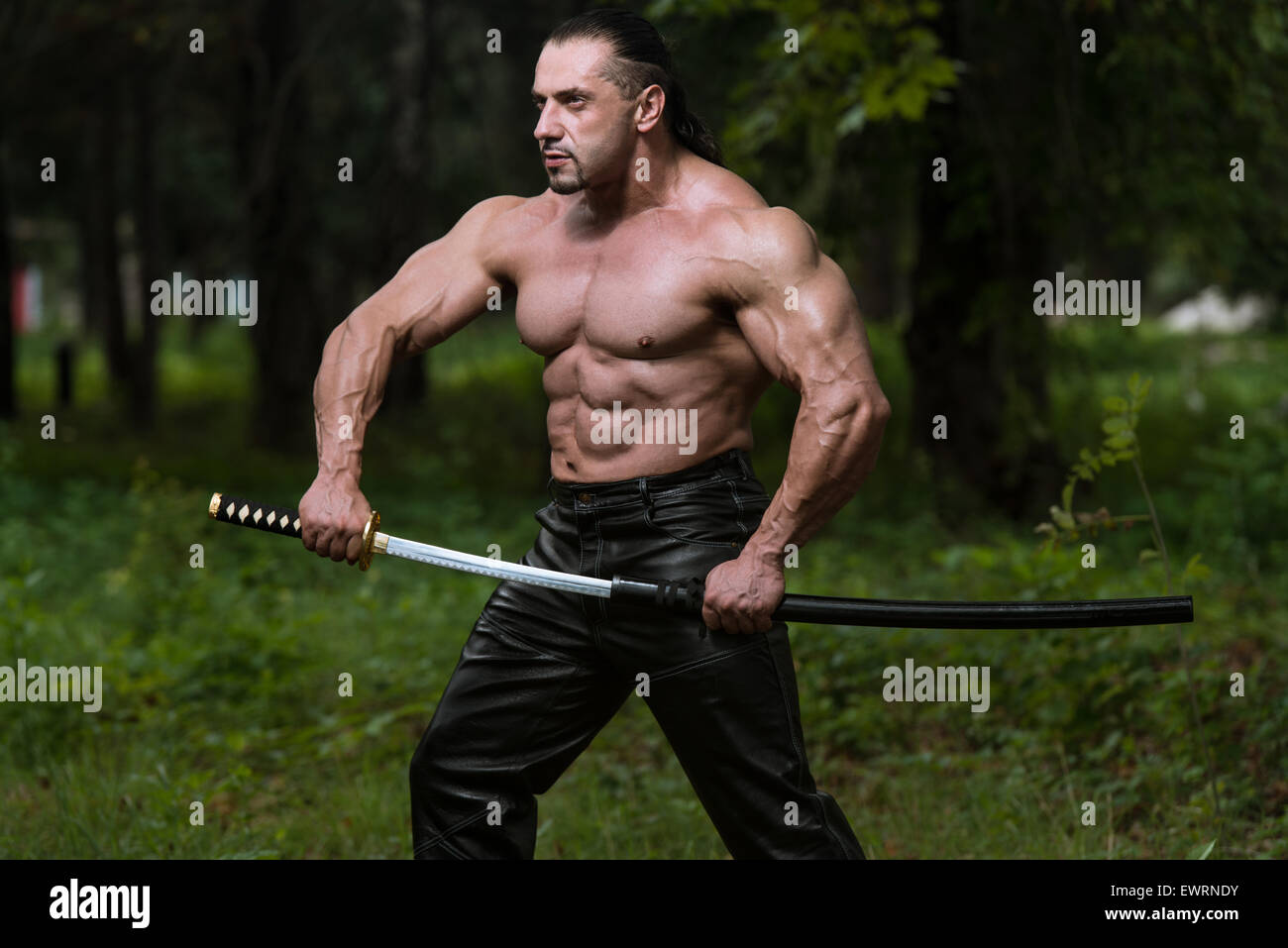 Action Hero Muscled Man Holding A Ancient Sword - Standing In Forest ...