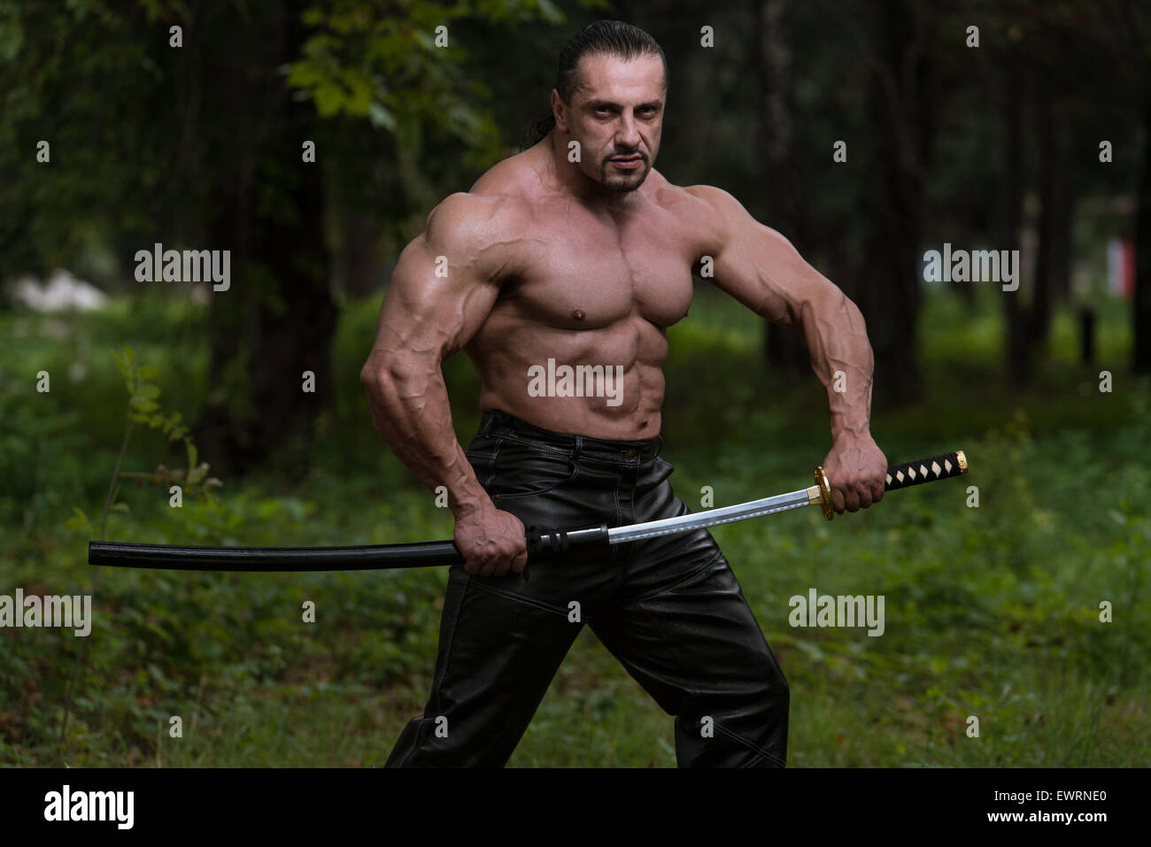 Action Hero Muscled Man Holding A Ancient Sword - Standing In Forest ...