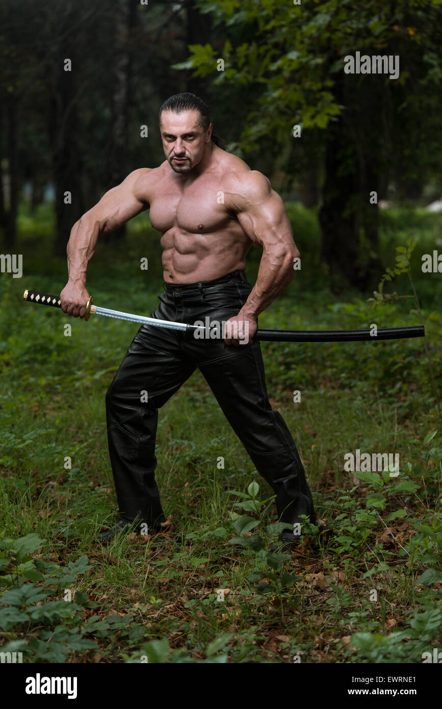 Action Hero Muscled Man Holding A Ancient Sword - Standing In Forest ...