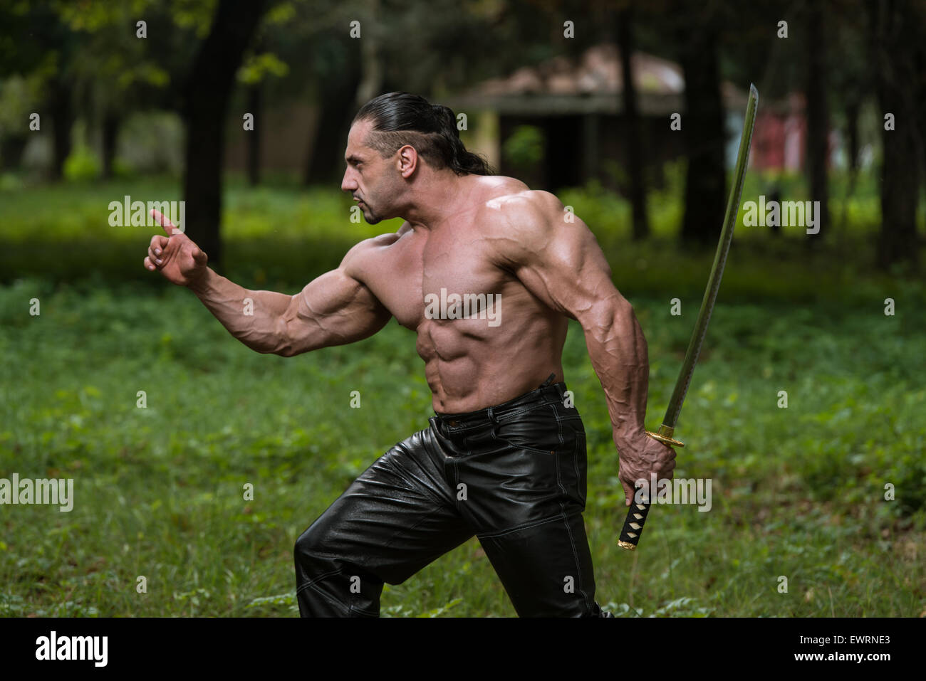 Action Hero Muscled Man Holding A Ancient Sword - Standing In Forest ...