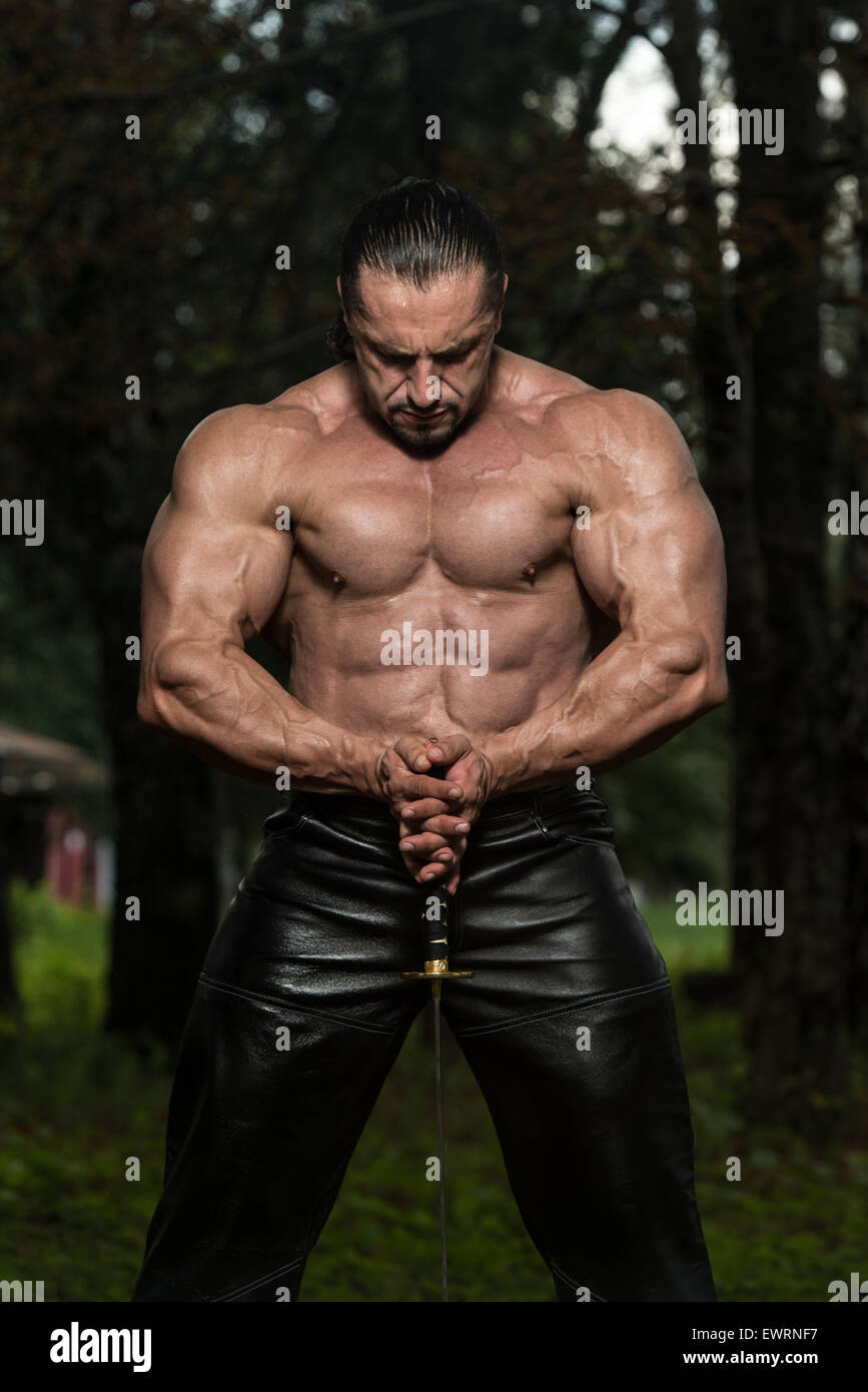 Action Hero Muscled Man Holding A Ancient Sword - Standing In Forest ...