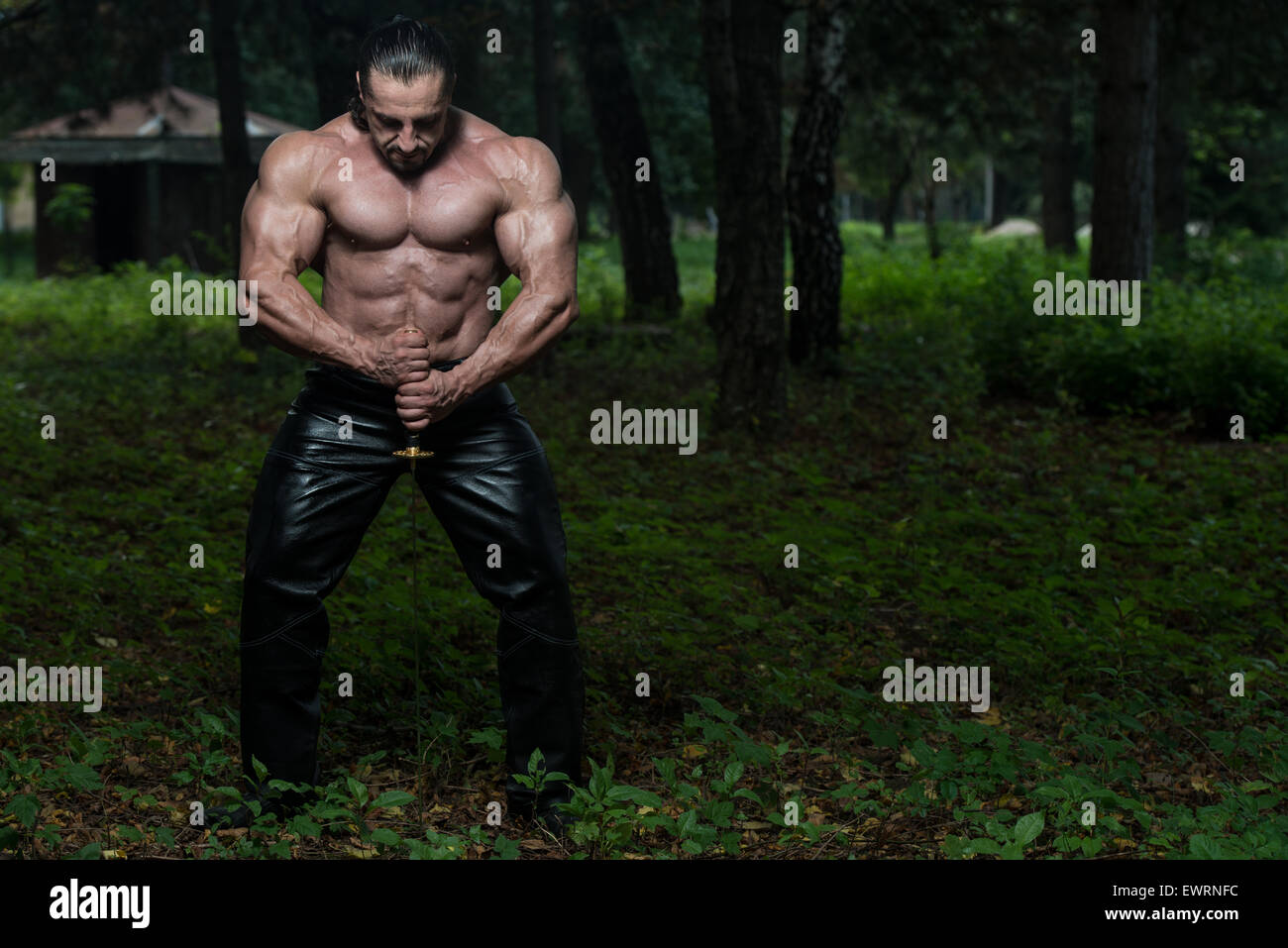 Action Hero Muscled Man Holding A Ancient Sword - Standing In Forest ...