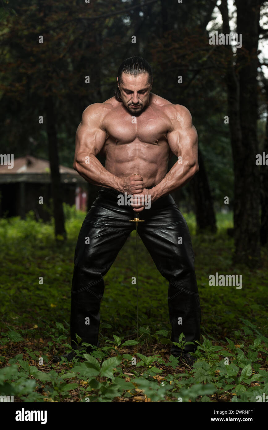 Action Hero Muscled Man Holding A Ancient Sword - Standing In Forest ...