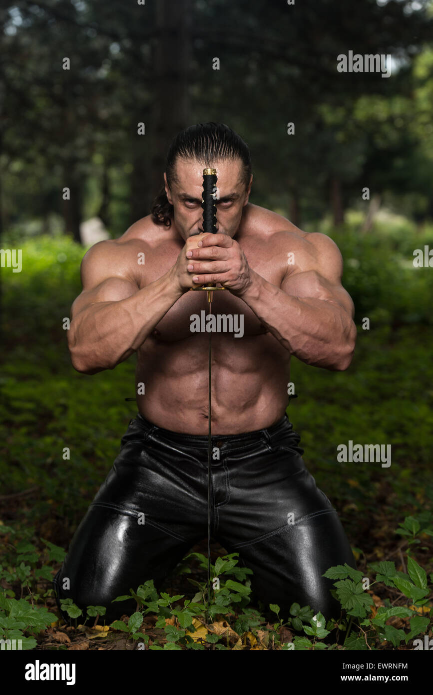 Action Hero Muscled Man Holding A Ancient Sword - Standing In Forest ...