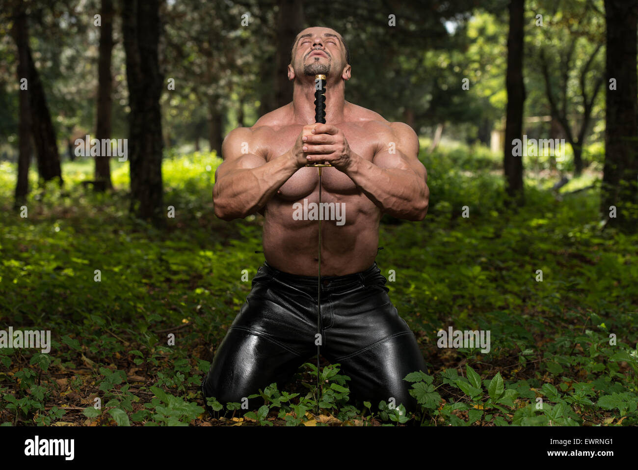 Action Hero Muscled Man Holding A Ancient Sword - Standing In Forest ...
