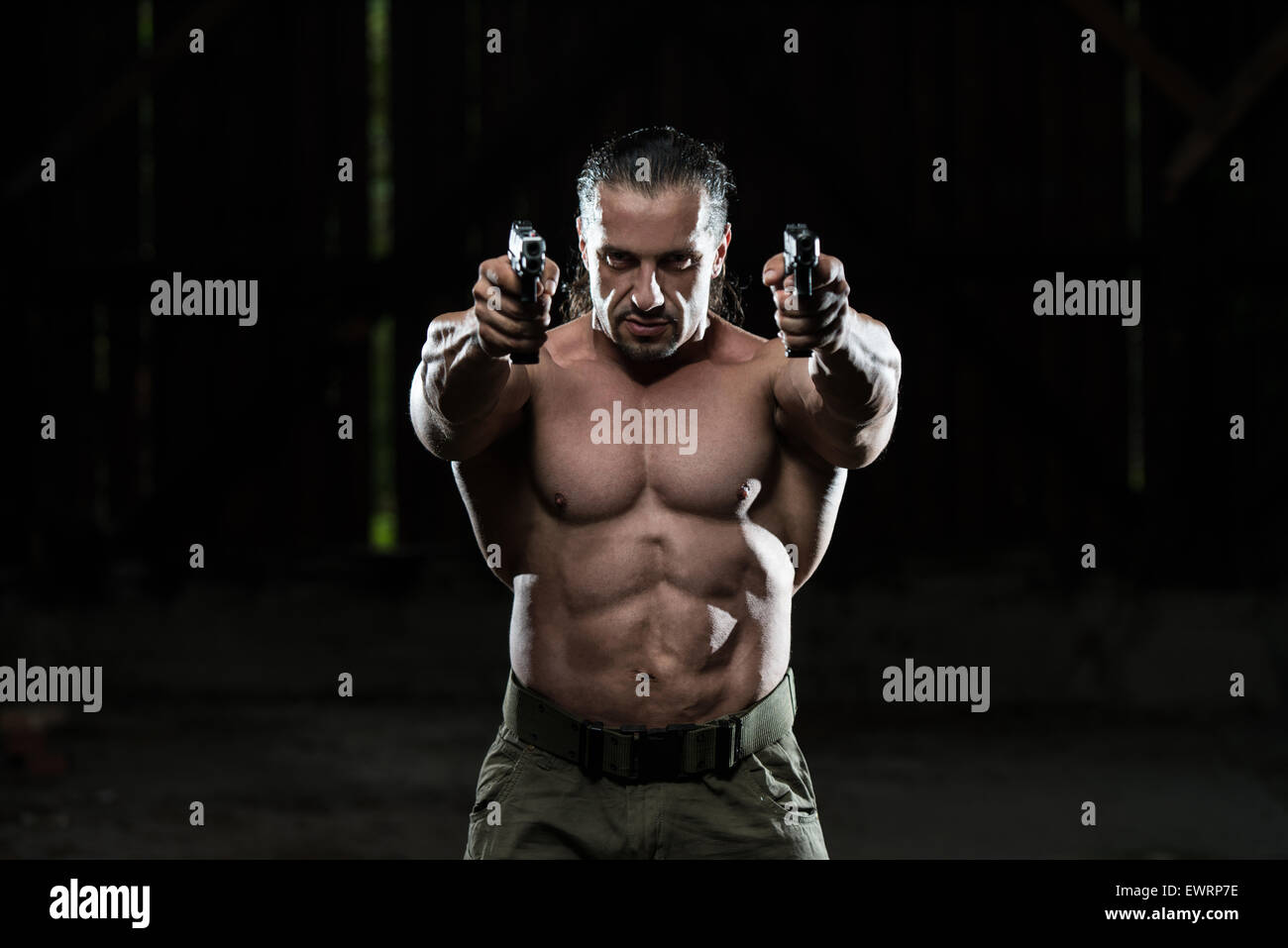 Action Hero Muscled Man Holding Two Guns - Standing In Abandoned ...