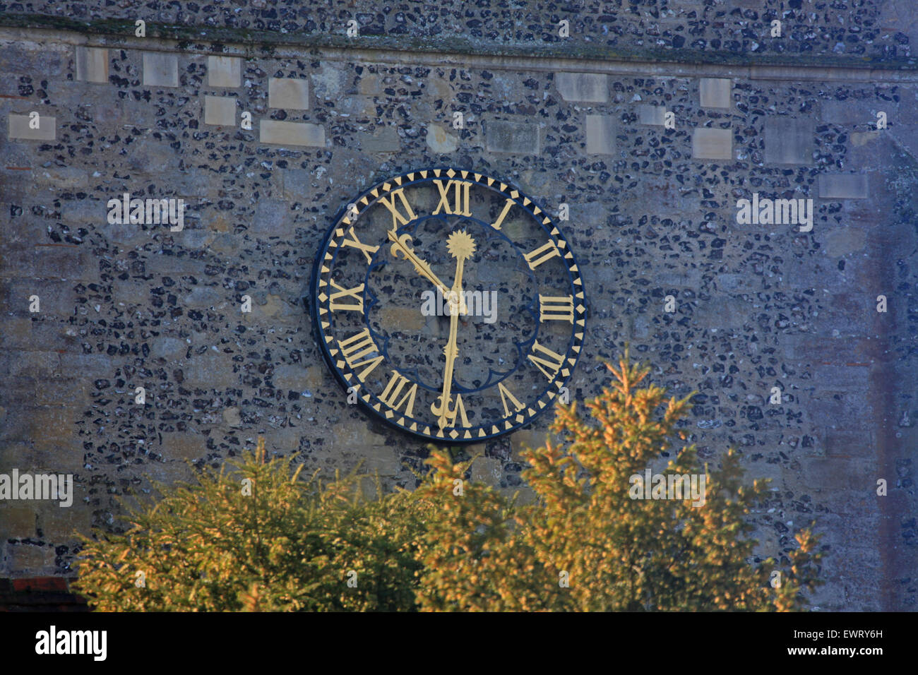 A church wall clock with Gold numbers and hands on a flint and block ...