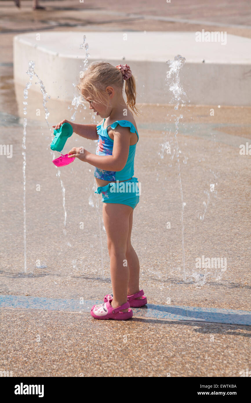 Young girl enjoys the cooling water in the new water fountain feature ...