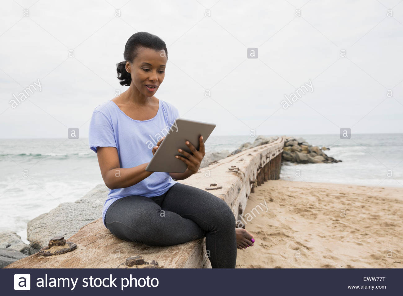 Woman using digital tablet on beach jetty Stock Photo - Alamy