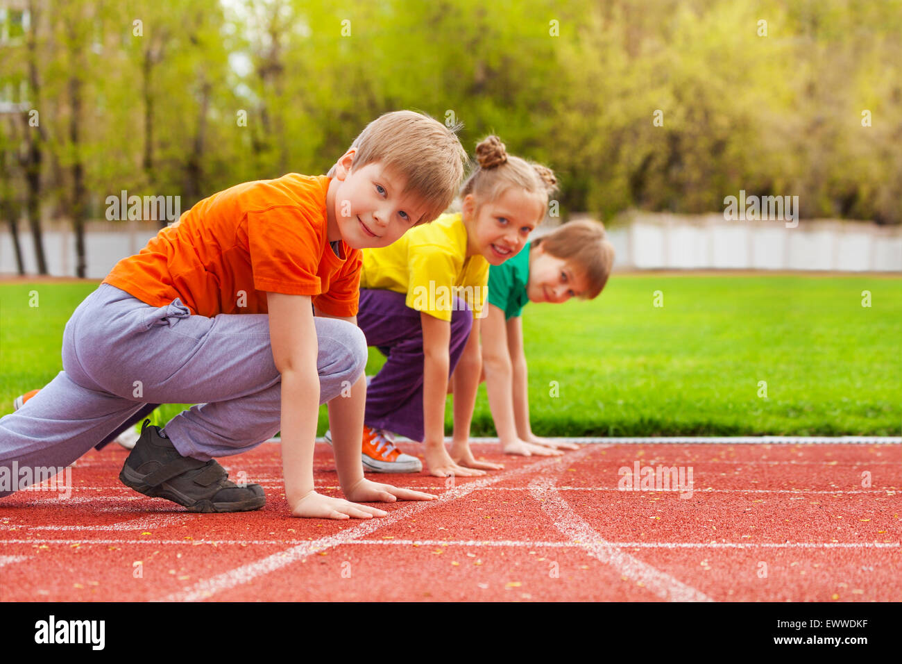 Two boys and girl stand on knee ready to run Stock Photo - Alamy