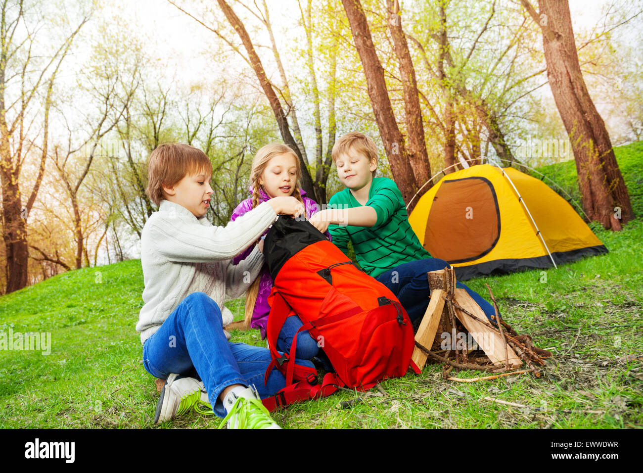 Three kids packing the things into red rucksack Stock Photo - Alamy
