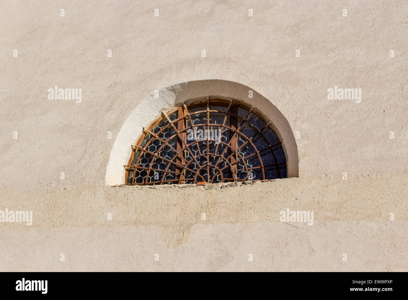 Rounded stone window with grate of rusty brownish iron bars on wood ...