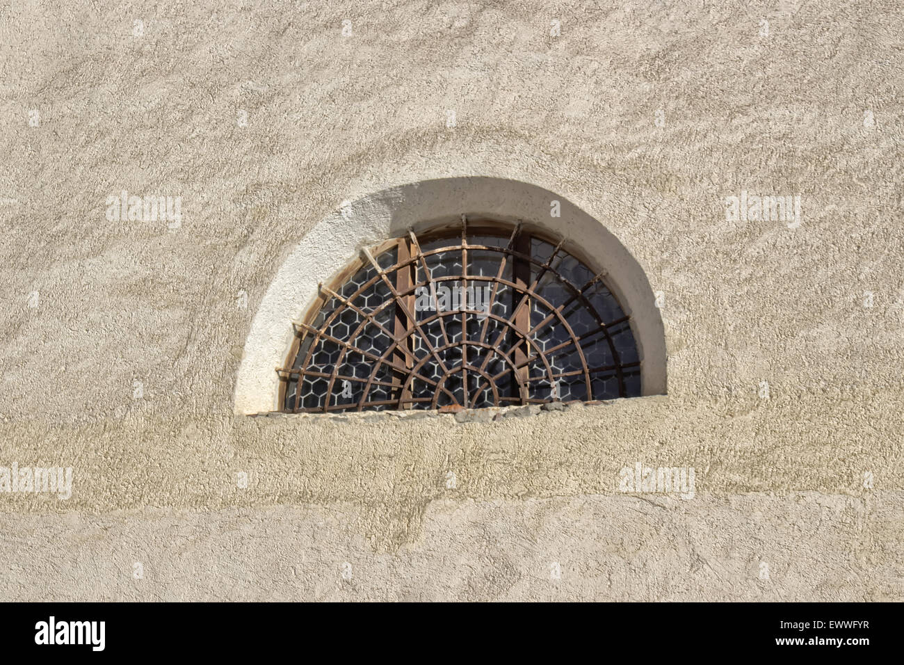 Rounded stone window with grate of rusty brownish iron bars on wood ...