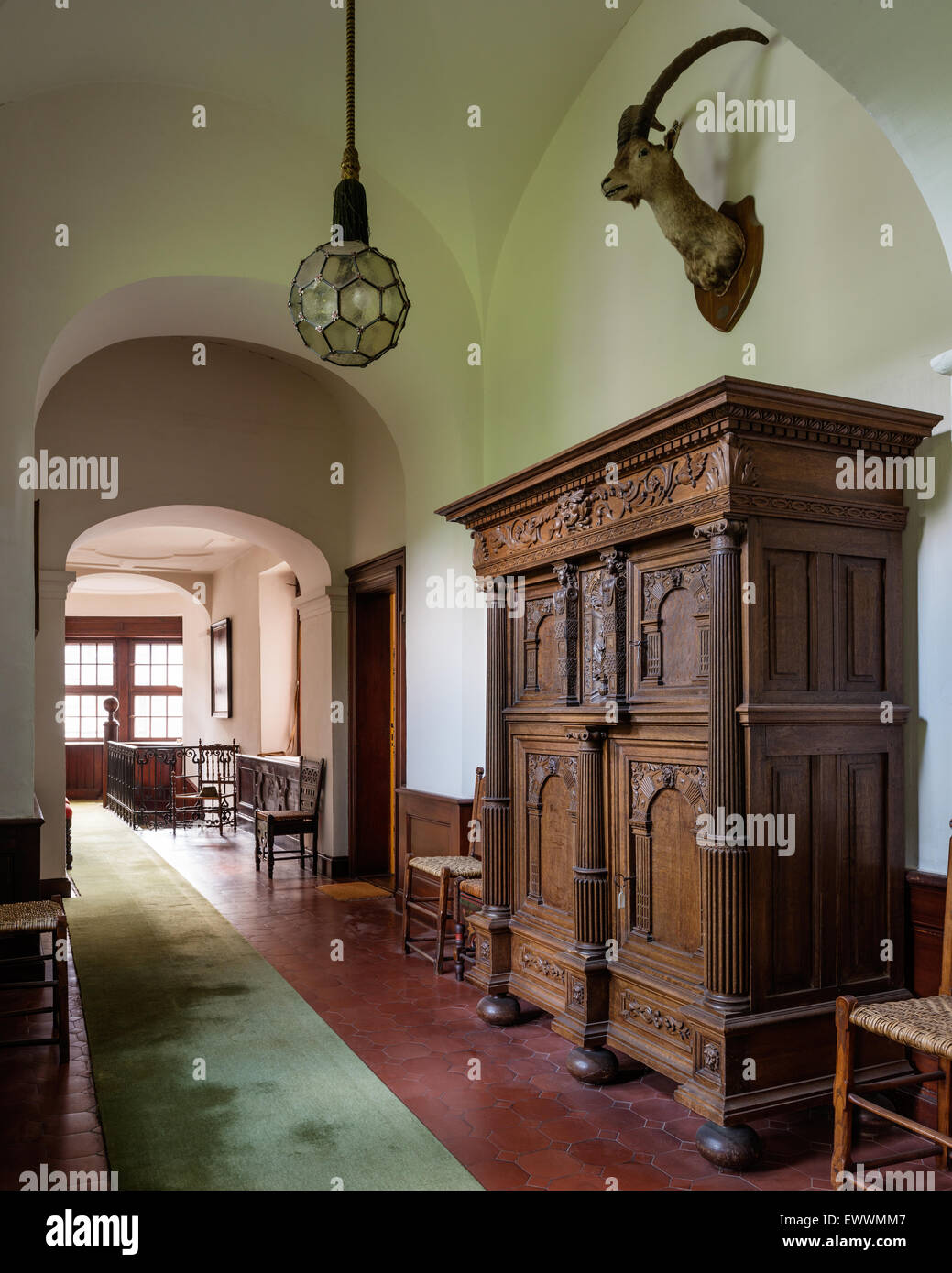 Ornate carved wooden cupboard in long arched corridor with mounted head ...