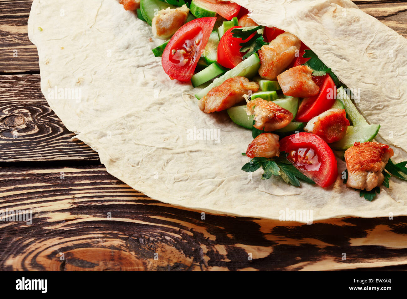 Traditional shawarma wrap with chicken and vegetables on wooden table ...