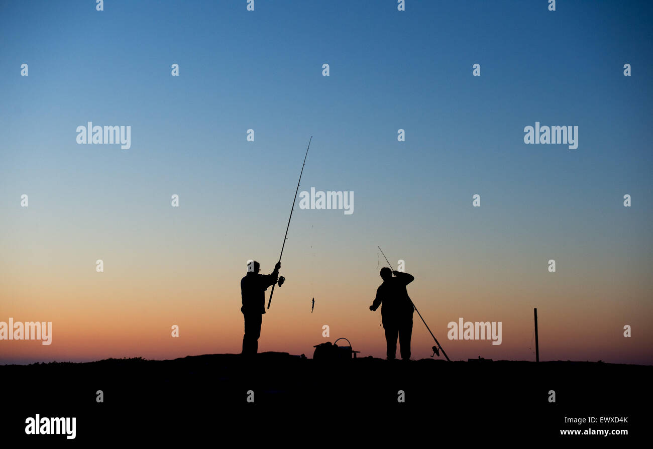 Two fisherman stand against the evening sky at the mouth of the habour ...