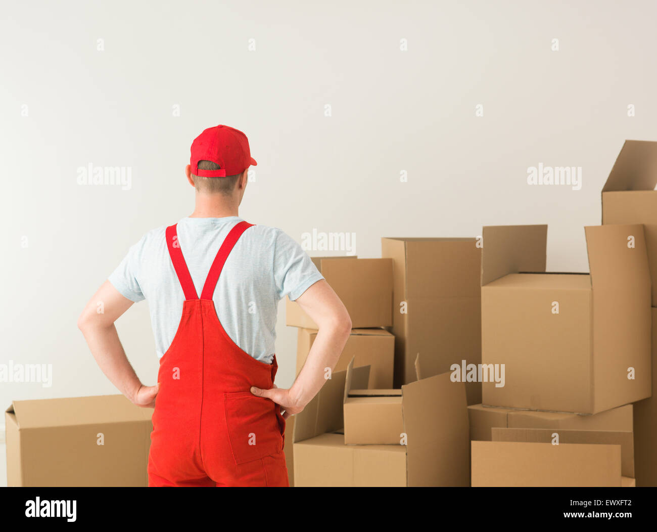rear view of deliveryman standing, looking at cardboard boxes in front ...