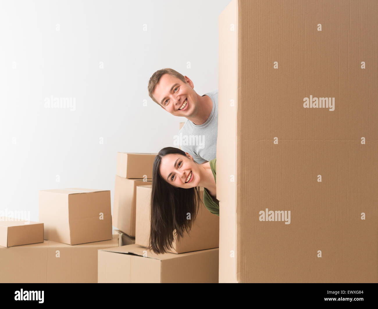 young happy couple hiding behind box, having fun during moving in new ...
