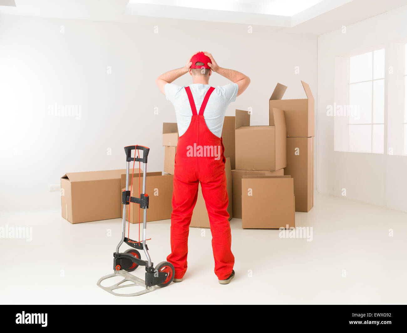 rear view of delivery man facing pile of cardboard boxes, holding his ...