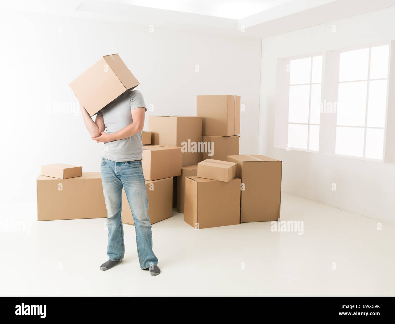 man hiding his head in cardboard box, standing in new apartment ...