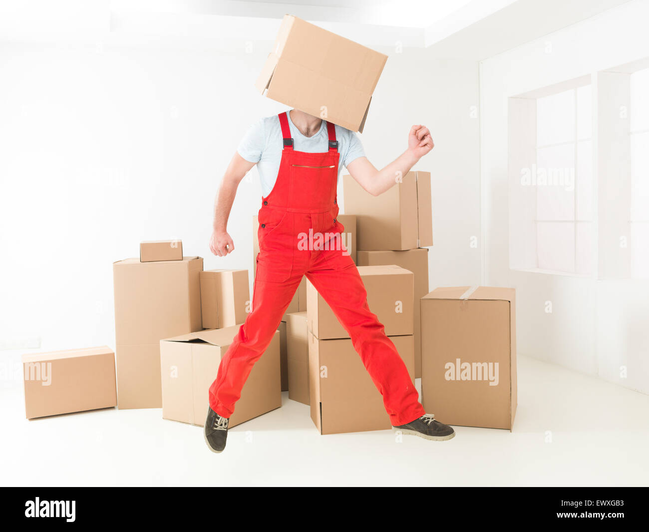 overjoyed delivery man jumping in warehouse with box covering his head ...