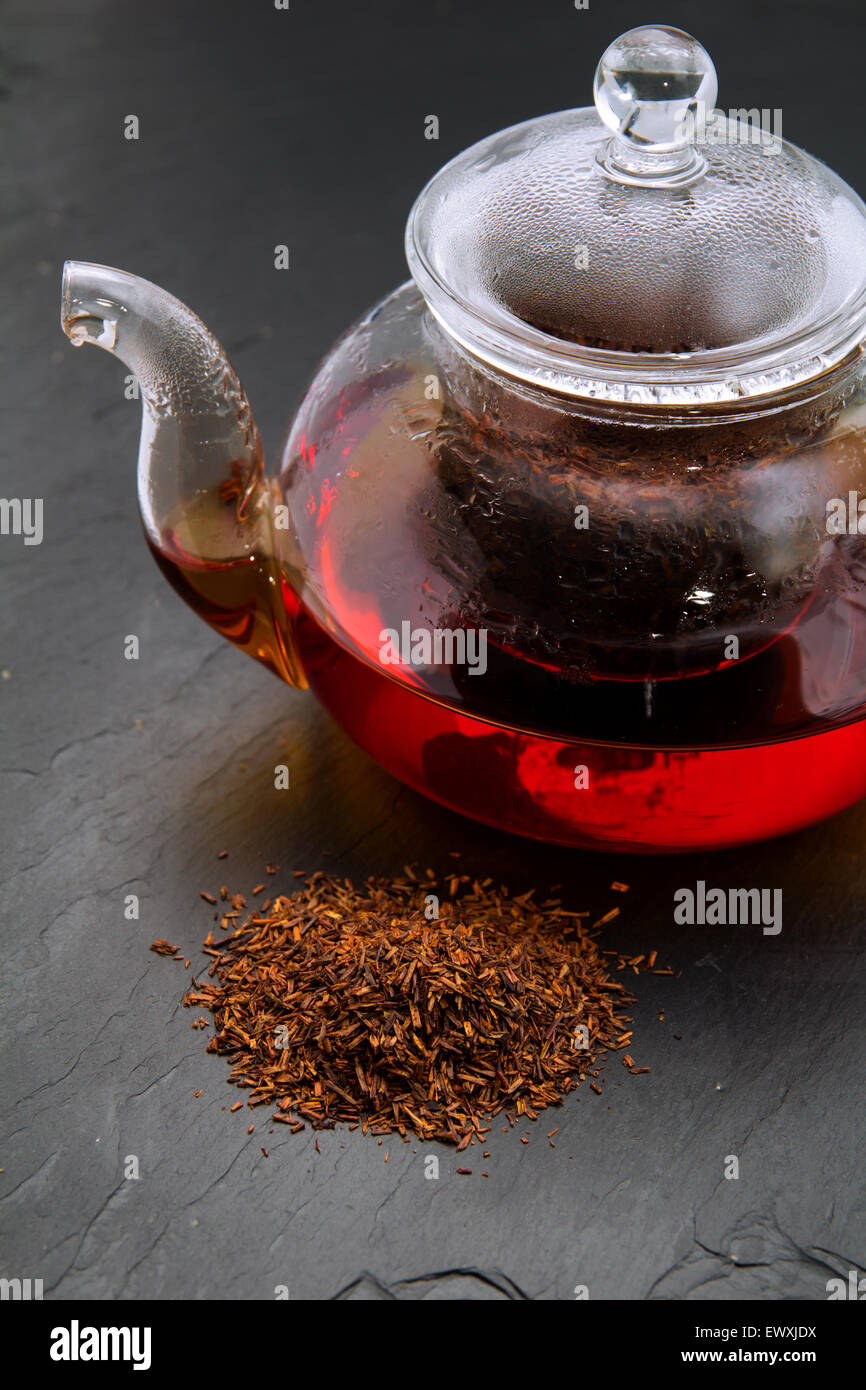 Rooibos tea, dry leaves and a small glass teapot brewing, on black ...