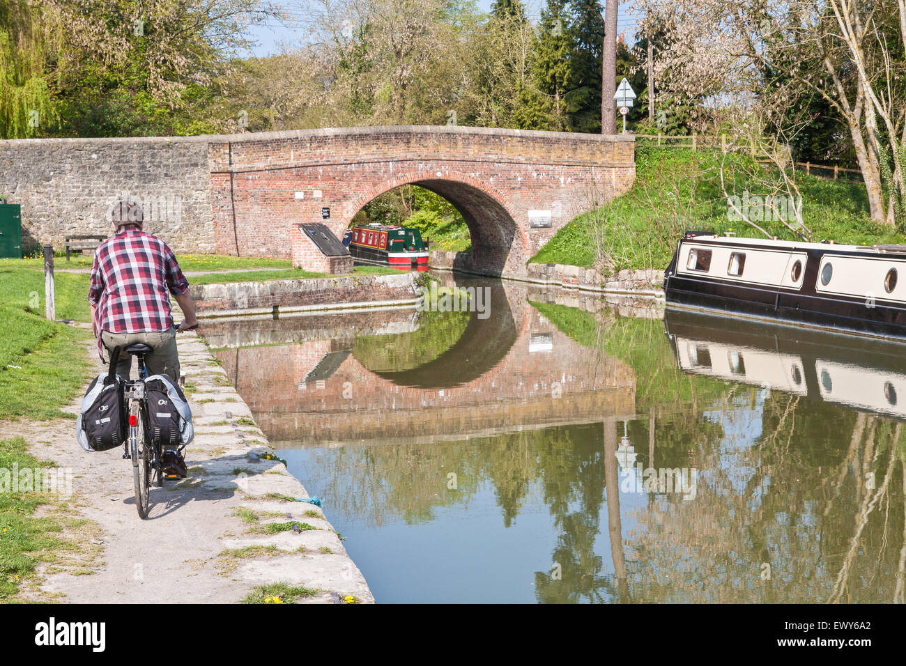 Cyclist cycling along canal side passing narrowboat. Part of the Kennet ...