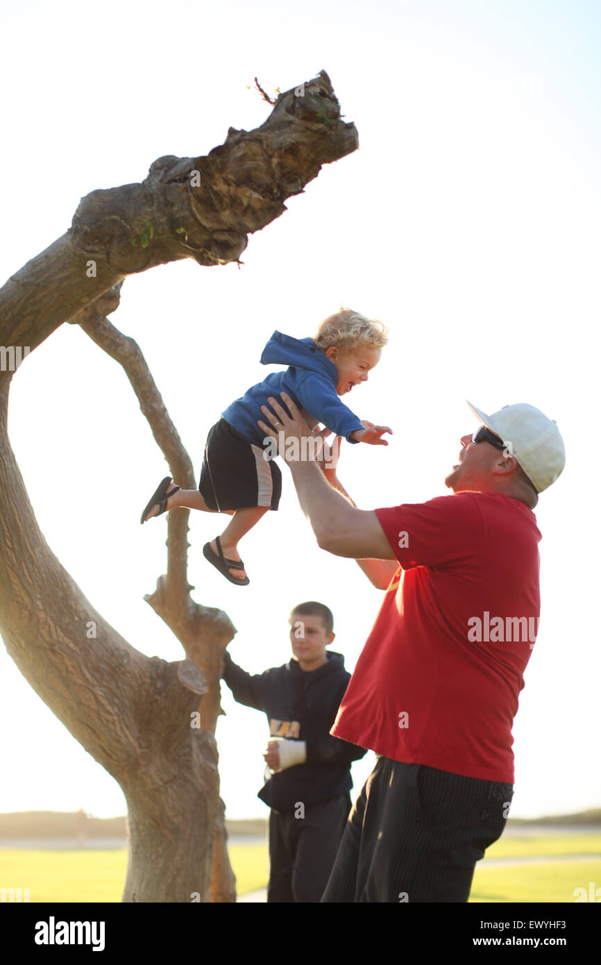 Father catching son jumping off a tree trunk with boy in background ...