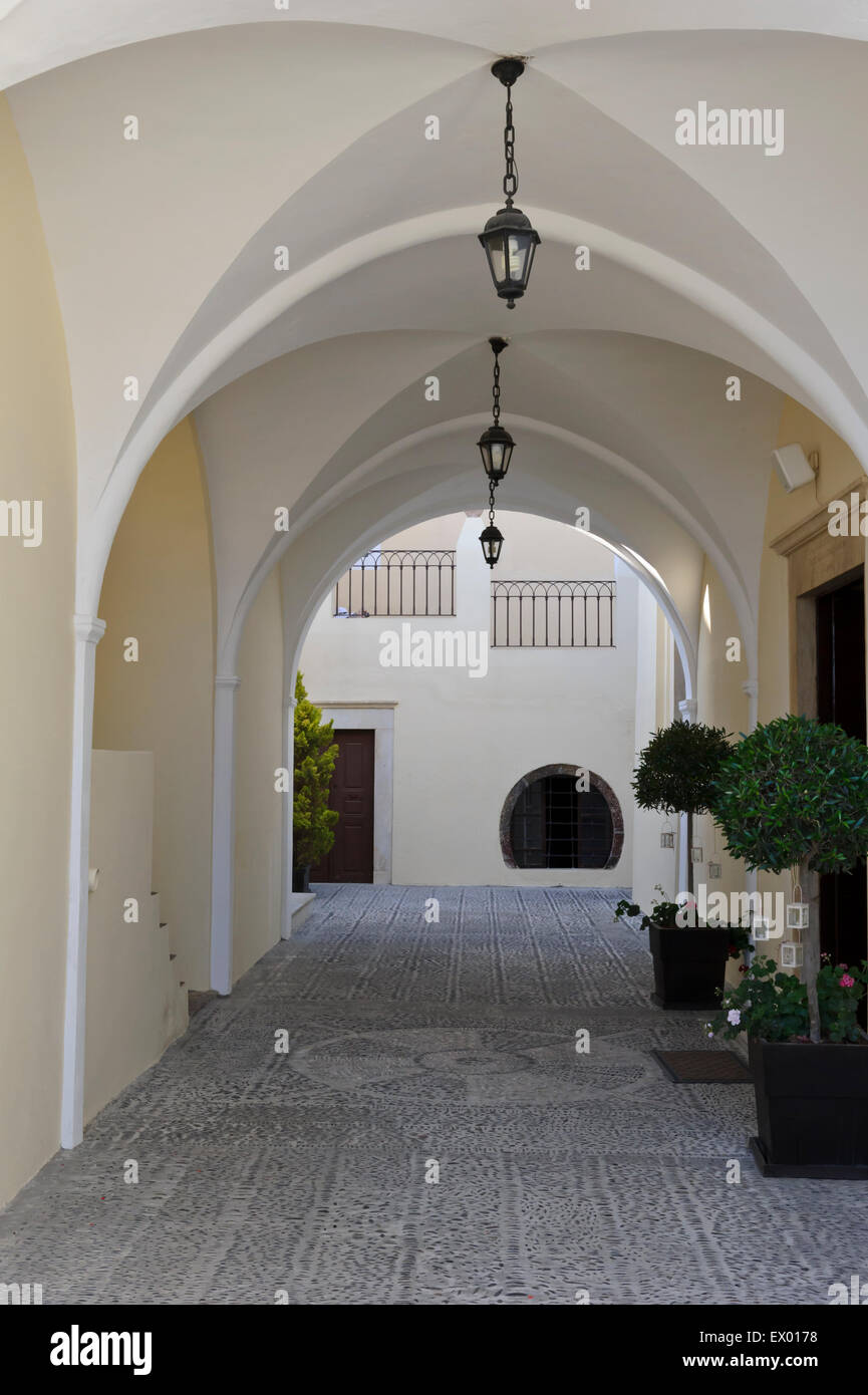 A corridor with arches and cobbled pavement outside a church in Fira ...