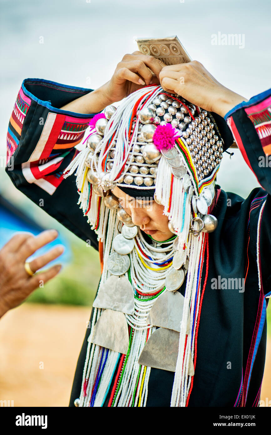 Young Akha woman being helped to put on her traditional clothing in Mae ...