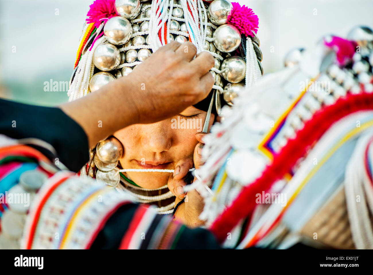 Young Akha woman being helped to put on her traditional clothing in Mae ...