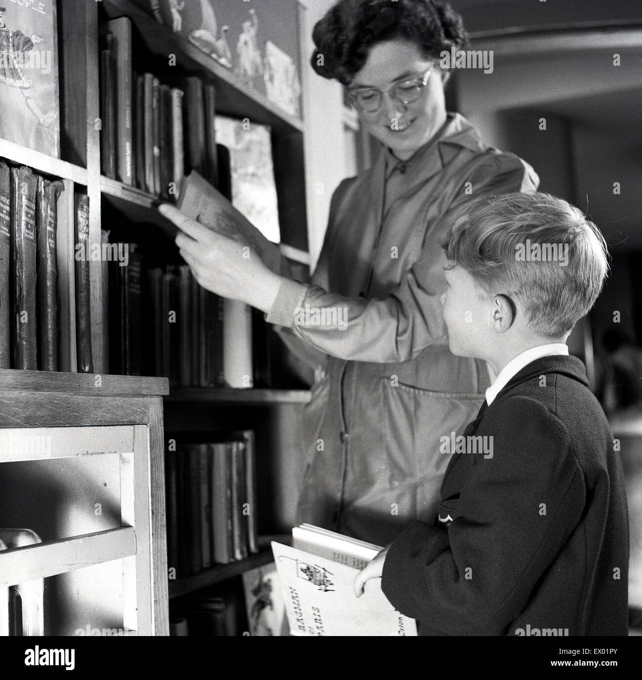 Historical, 1950s, female library assistant shows a young boy some ...